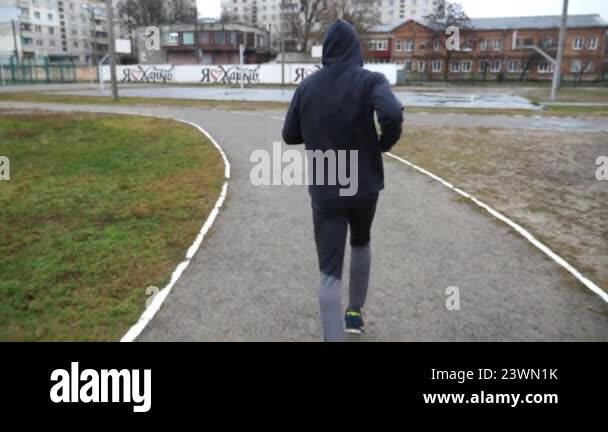 Athletic sporty man jogging at track on school stadium in cloudy day ...