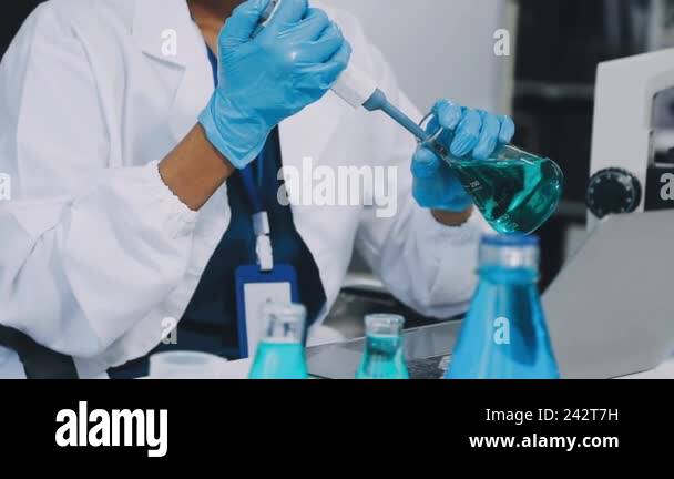 scientist in blue uniform and gloves working with chemical flask in ...