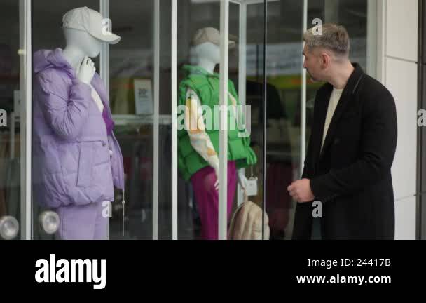 A man in a dark coat thoughtfully examines a storefront display ...