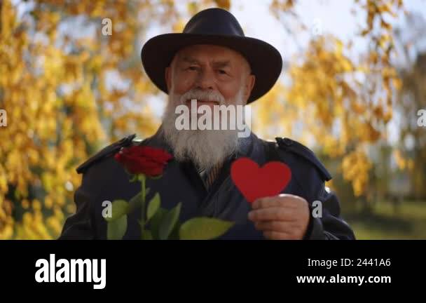 A bearded man wearing a stylish hat lovingly holds a beautiful rose and ...