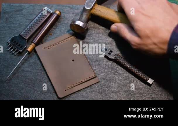 A close-up of an artisan hand picking tools for making a leather wallet ...