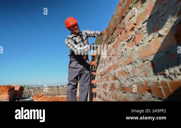 A skilled bricklayer wearing safety gear applies mortar to bricks while ...