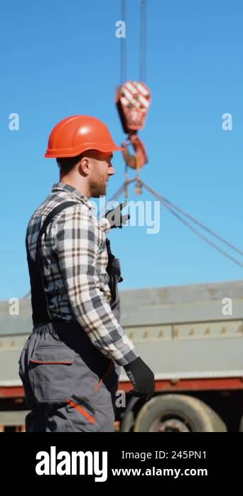 A foreman in a hard hat signals to a crane operator while lifting a ...