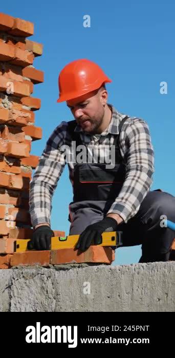 A construction worker in safety gear carefully lays bricks, building a ...