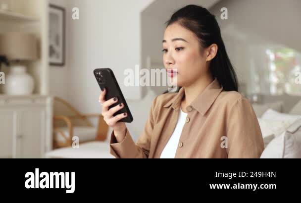 Focused beautiful young Asian woman scrolling mobile phone, reading ...