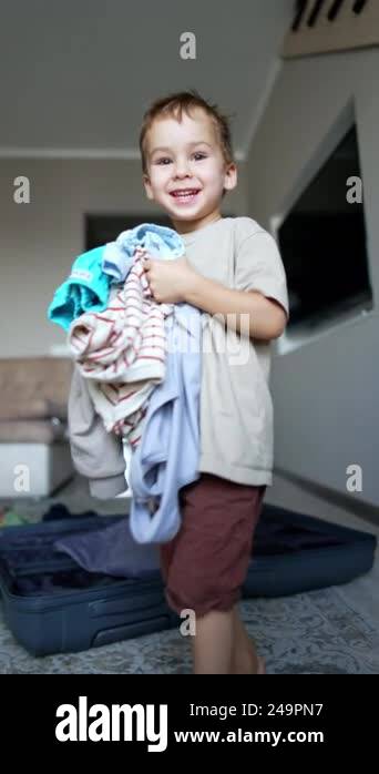 Smiling kid holds few of his clothes in his hands. Toddler comes up to ...