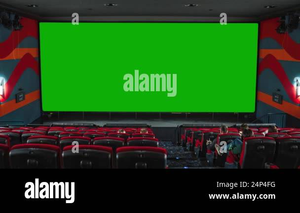 People sitting in cinema theater chairs watching big green screen ...