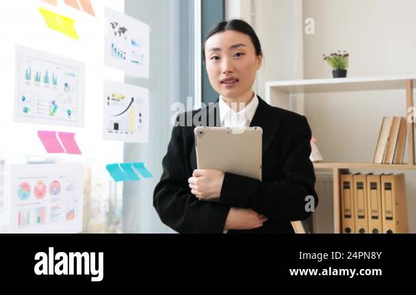 Confident Asian businesswoman holding tablet, making okay gesture in modern office. Engaged in ...