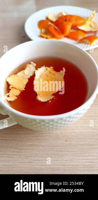 A hand puts a mandarin peel in hot tea. Tea with a crust of tangerine ...