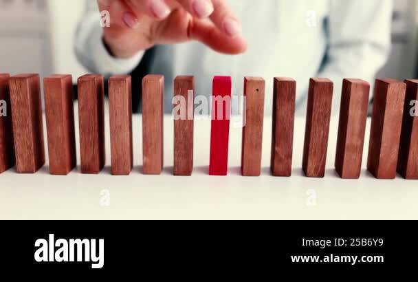 A hand poised to push a red domino among brown ones, symbolizing change ...