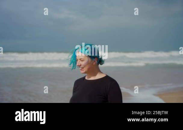 A woman with blue hair strolls along a deserted beach, with gentle ...