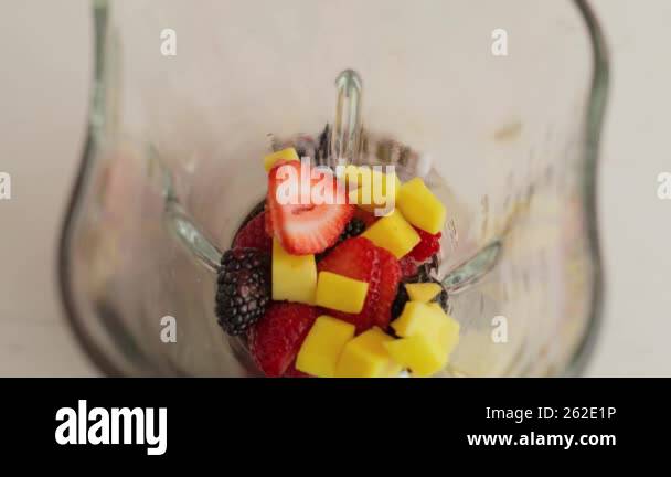 Close view of the inside of a blender as a woman blends strawberries ...