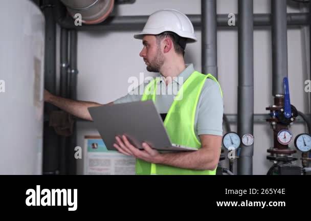 Serious male engineer in hardhat and uniform checks readings on laptop ...