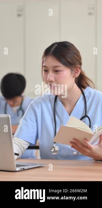 Smiling female medical student wearing scrubs working with her laptop ...