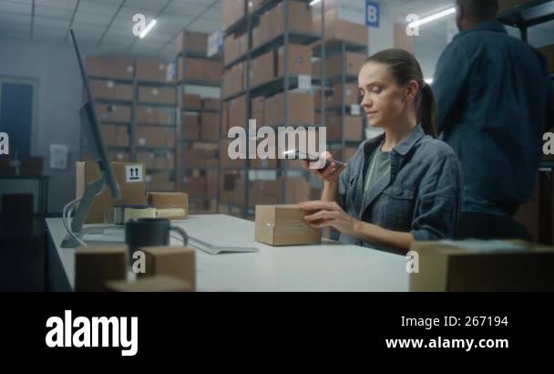 Female logistics manager scans parcel using smartphone, enters information on computer, works in ...