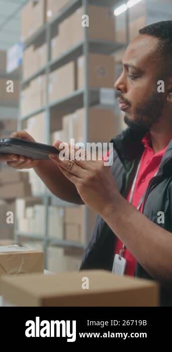 African American warehouse clerk scans parcel using tablet computer ...