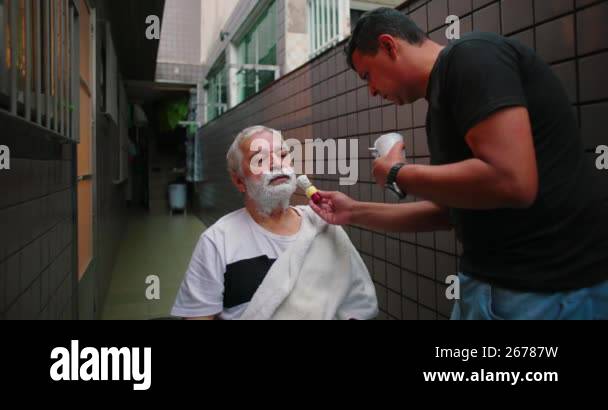 Son carefully shaving father face with foam and straight razor at home ...