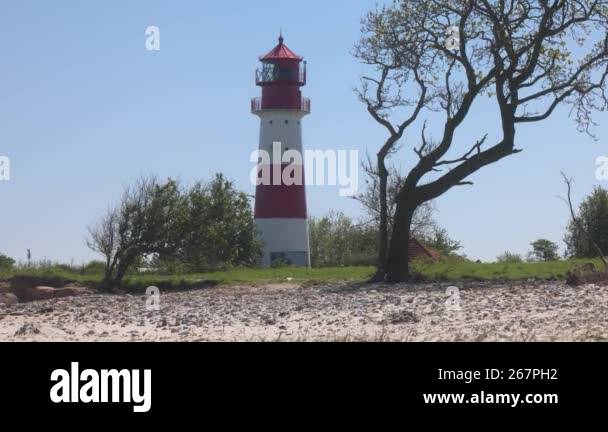 Red and white lighthouse in Pommerby on a cliff overlooking a beach ...
