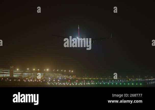 Airplane descends onto a brightly lit airport runway at night ...