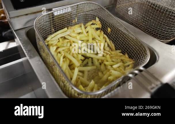 French fries frying in boiling oil inside a professional deep fryer ...