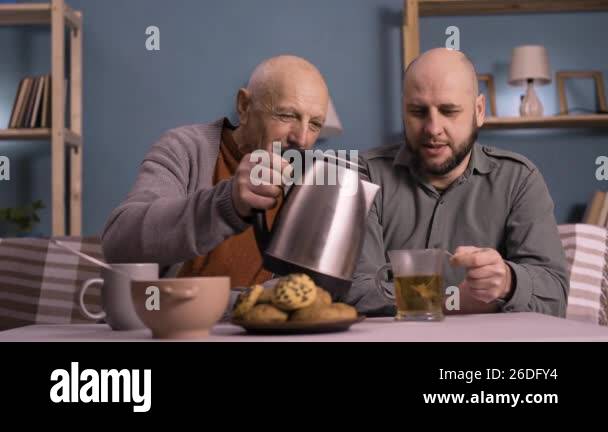 Young adult man drinking tea with his elderly father sitting in the ...