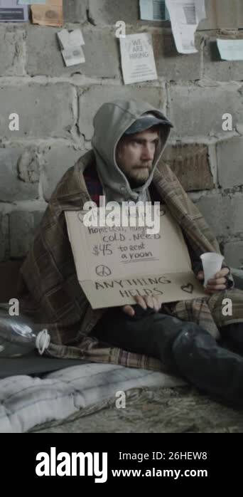 Vertical view of homeless man sitting on street with cardboard sign and ...