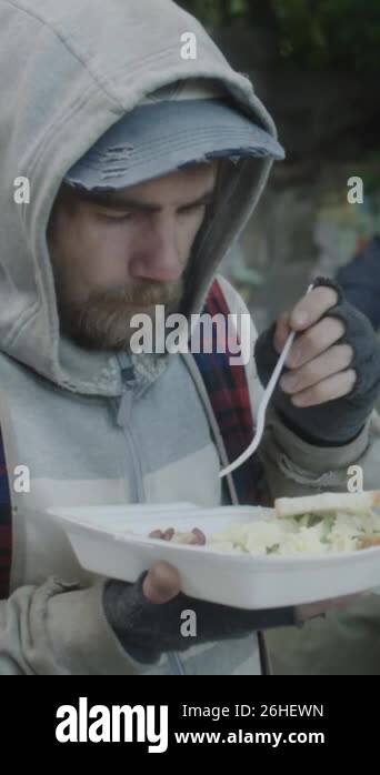 Vertical view of homeless man holding disposable container and eating ...