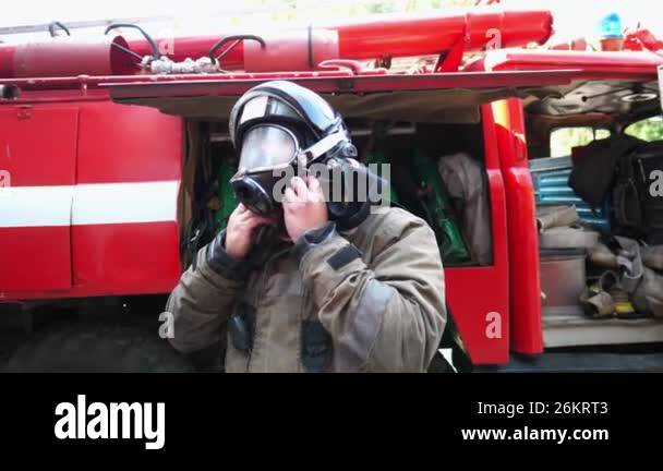Male firefighter taking off helmet and balaclava stands near fire ...