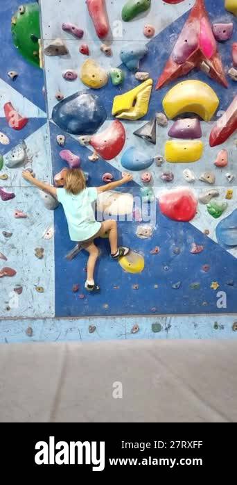 A child climbing a colorful indoor rock wall, showcasing strength ...
