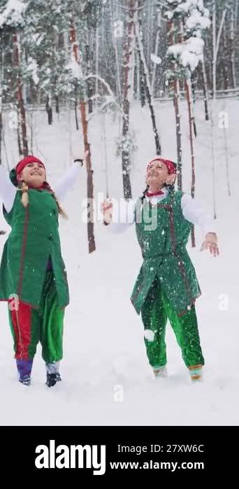Funny elves in green suits with hats are throwing up snow and looking ...