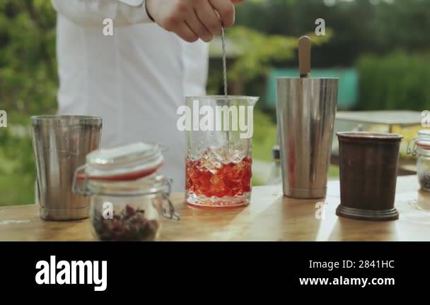 A bartender expertly mixes a vibrant cocktail outdoors, demonstrating ...