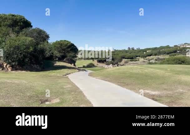 A golf course pathway surrounded by lush green trees and open grass ...