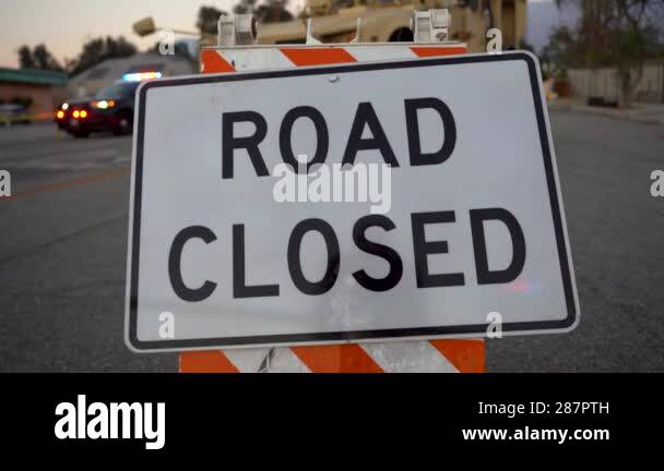 A prominent "Road Closed" sign, flanked by caution tape and a military ...