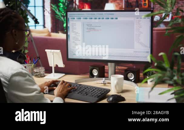 Woman in home office looking at UI on PC screen, typing and executing programming code. Coding ...