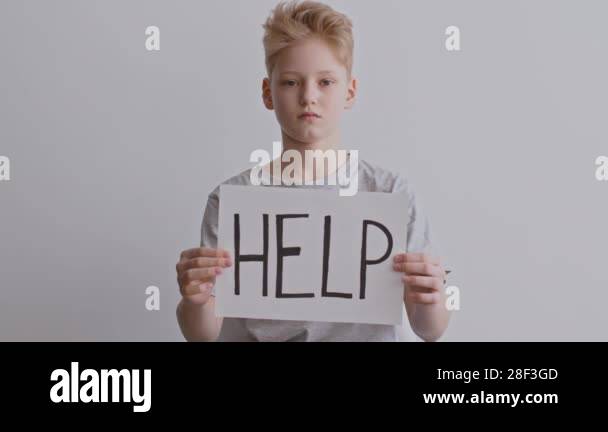 A young boy holds a sign reading help, looking serious and distressed ...
