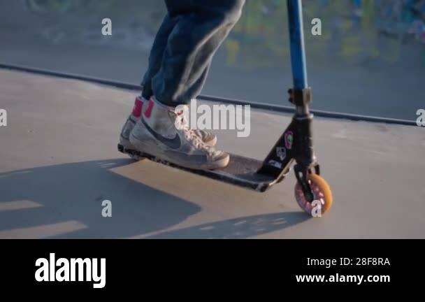 A close-up view of a persons feet on a scooter deck, wearing sneakers ...