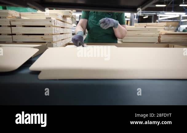 A worker in green overalls inspects wooden planks on a workstation in a ...