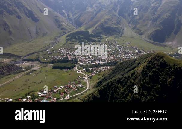 A small town sits in a valley surrounded by steep, rugged mountains in ...