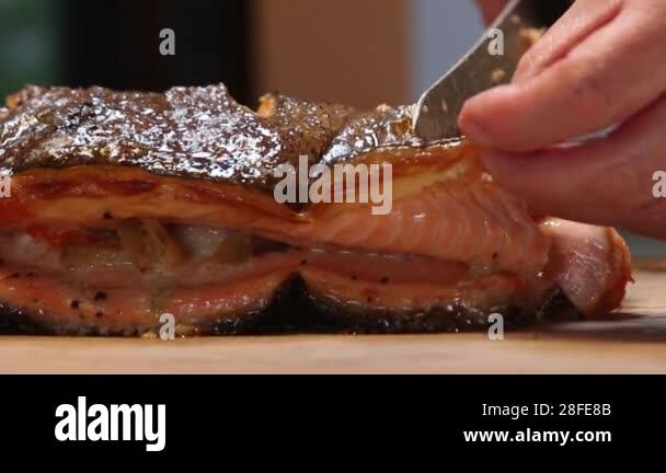 A knife slices through the tender, orange pink flesh of a roasted fish ...