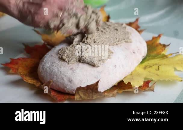 A loaf of bread dough rests on vibrant autumn leaves as a hand spreads ...