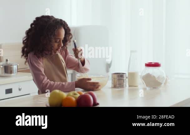 African American young girl uses a whisk to prepare a delicious mixture ...
