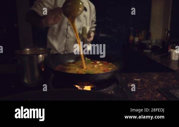 A chef in a white uniform cooks vegetables in a frying pan on a gas ...