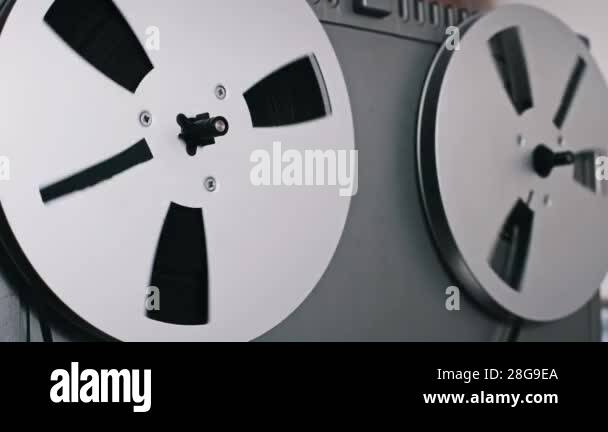 A vintage reel-to-reel tape deck with white reels is shown in close-up ...