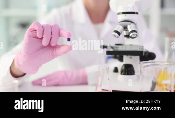 Lab assistant holds vibrant capsule-shaped tablet in hand. Professional ...