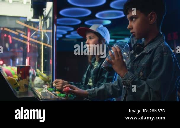 Medium shot of two diverse teenagers playing fighting video game together on machine at arcade ...