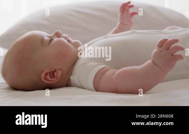 Side view of a baby boy in a white bodysuit lying on his back in a ...