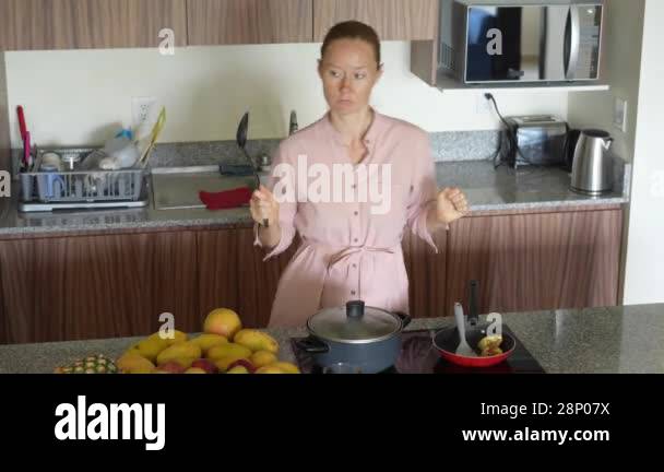 A young woman dances and sings joyfully while cooking in the kitchen. A ...