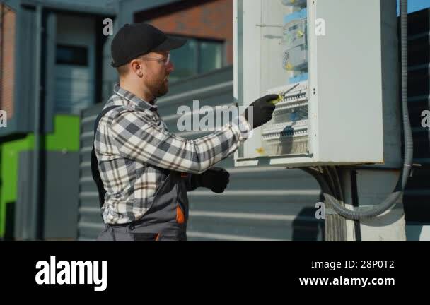 Side view of an electrician examining an outdoor electrical panel with ...