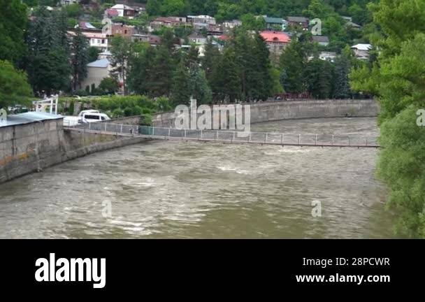 Powerful water rushes under narrow pedestrian suspension bridge ...