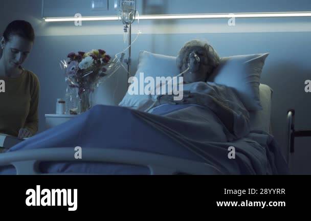 Young woman visiting her sick mother lying in a hospital bed, they talk ...